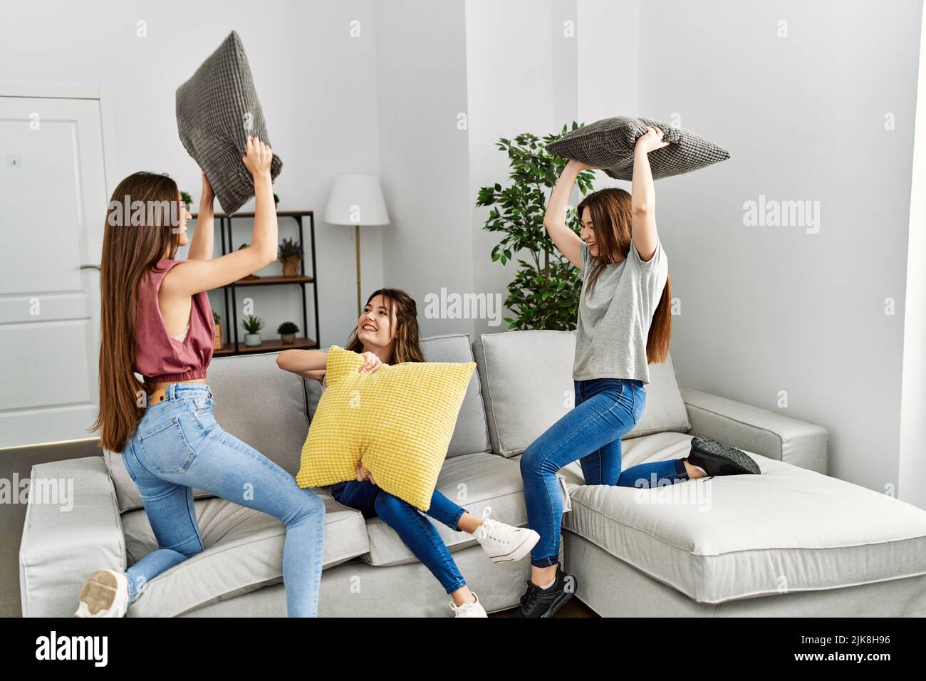 Three young hispanic woman smiling happy fighting with pillowa at home ...