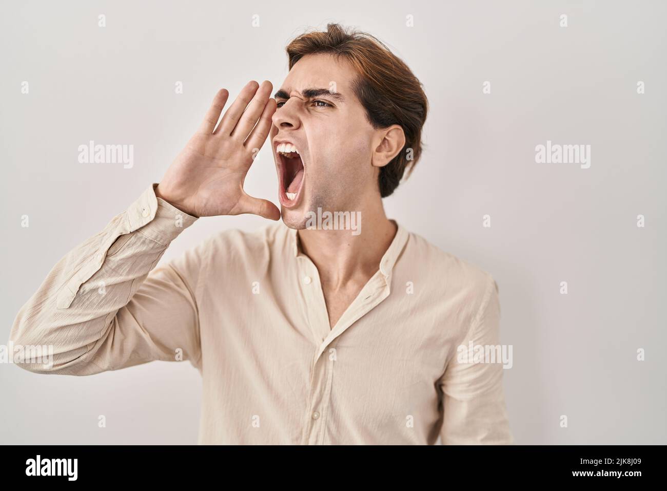Young man standing over isolated background shouting and screaming loud ...
