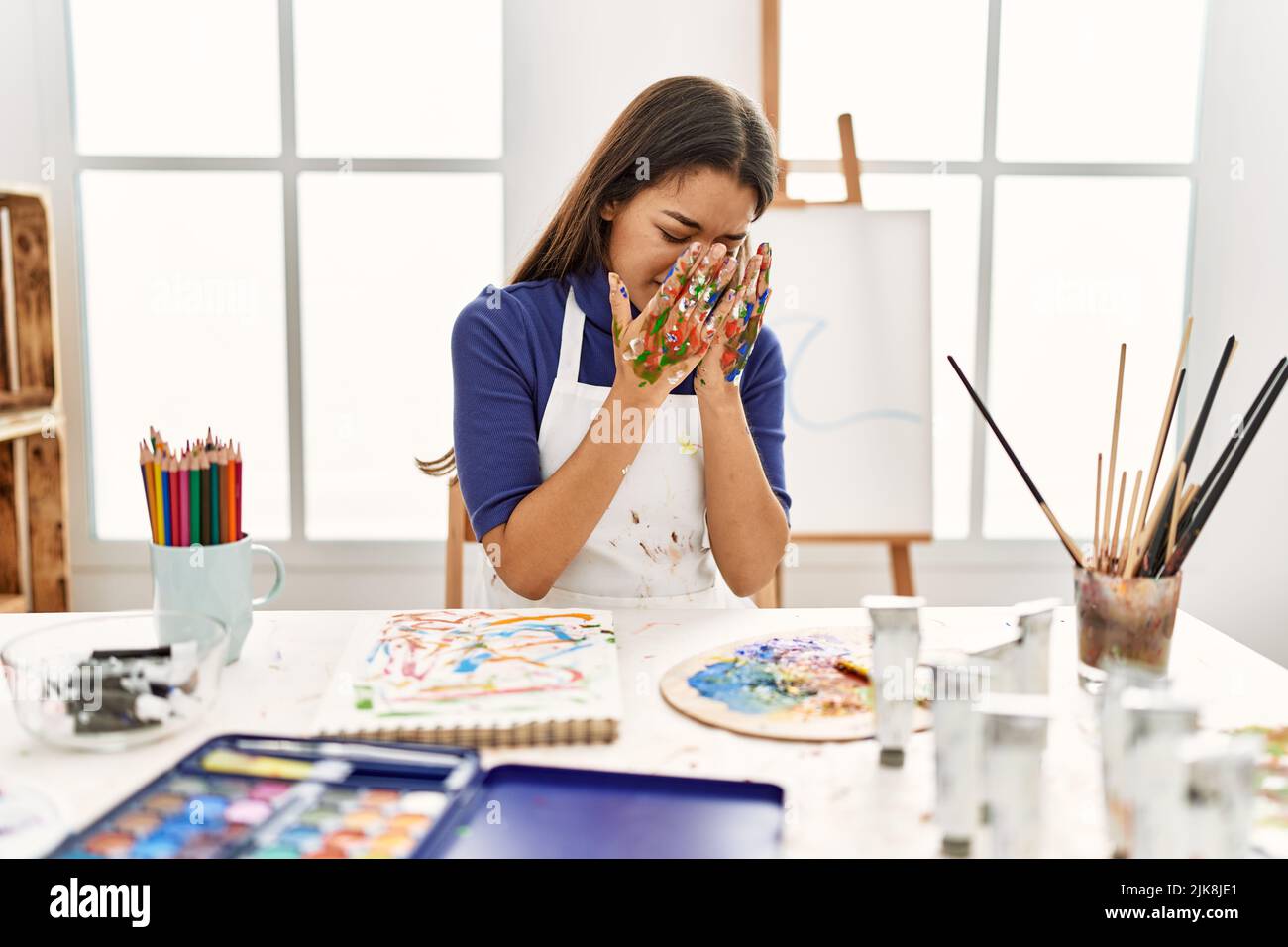Young brunette woman at art studio with painted hands with sad ...