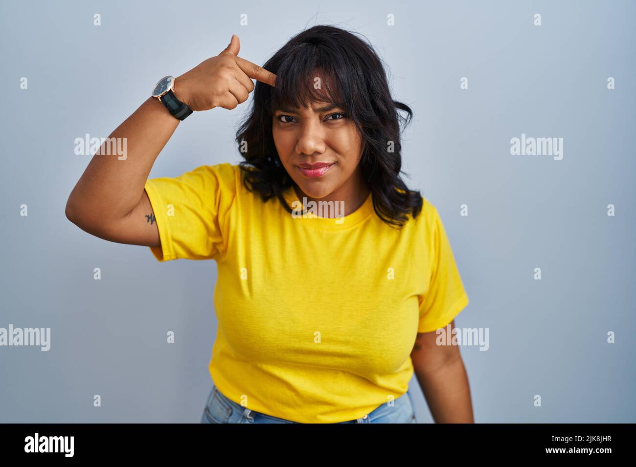 Hispanic woman standing over blue background pointing unhappy to pimple ...