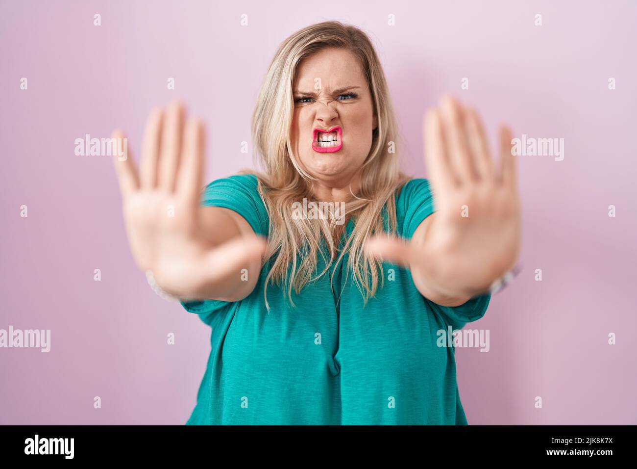 Caucasian plus size woman standing over pink background doing stop ...