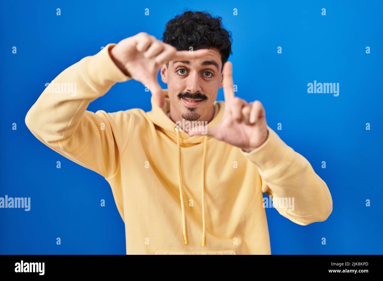 Hispanic man standing over blue background smiling making frame with ...