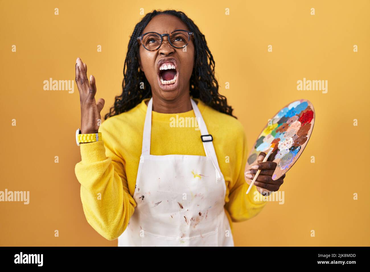 African woman holding painter palette crazy and mad shouting and ...