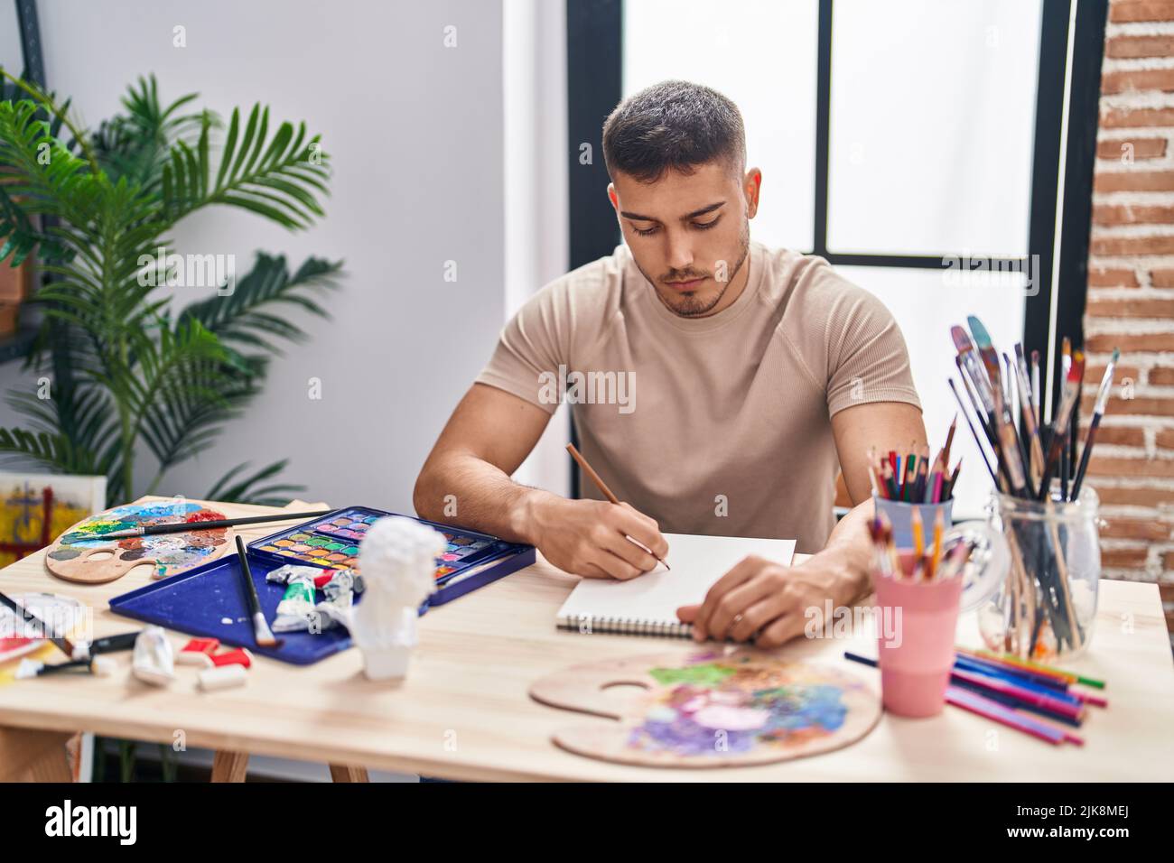 Young hispanic man artist drawing on notebook at art studio Stock Photo ...