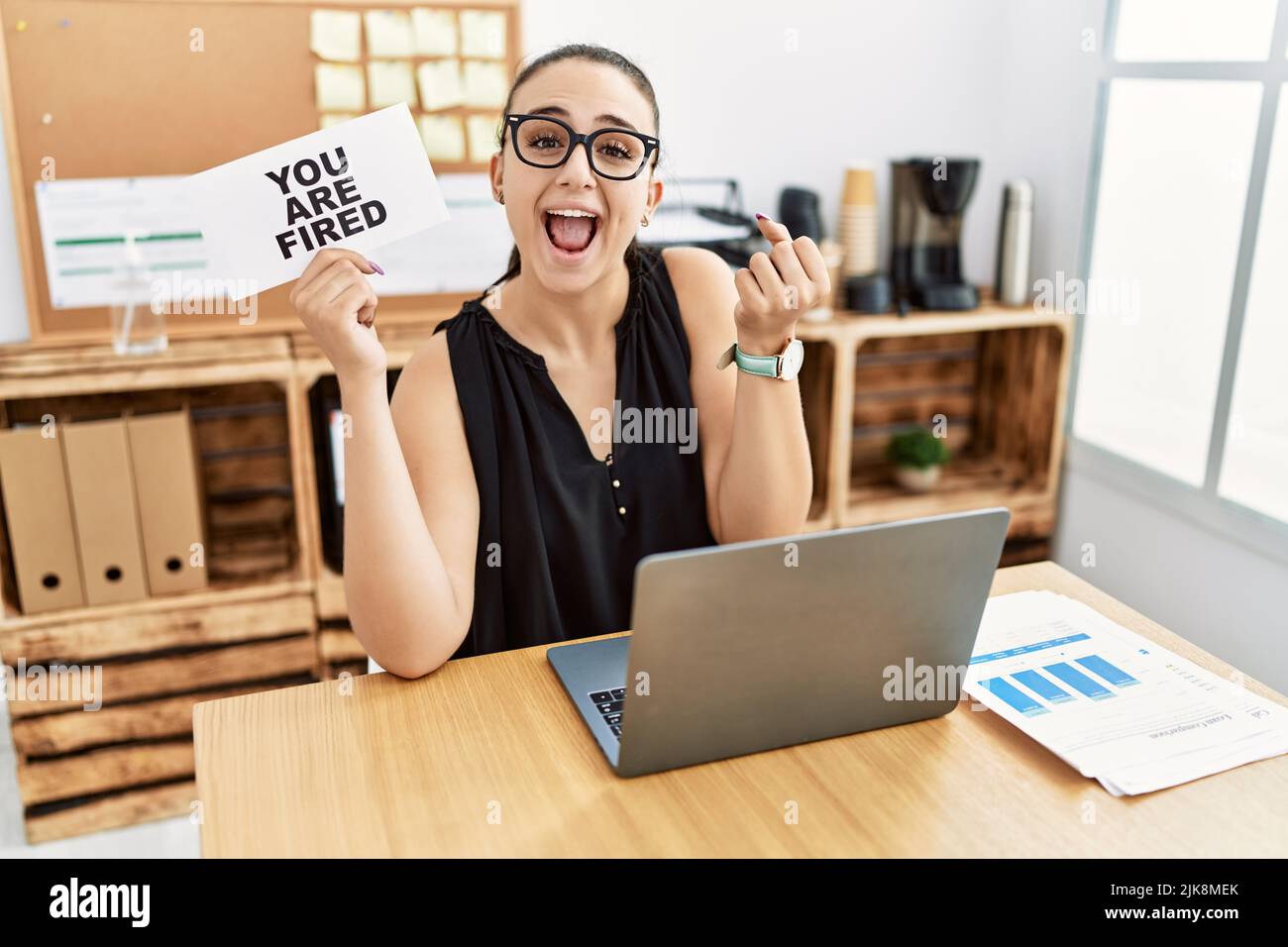 Young brunette woman holding you are fired banner at the office ...