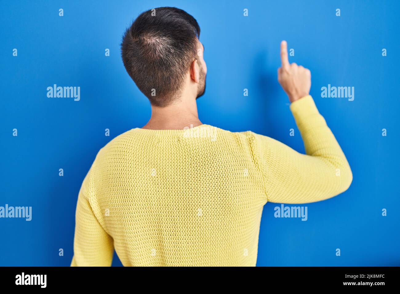 Hispanic man standing over blue background posing backwards pointing ...