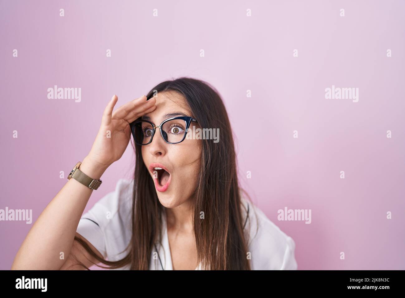 Young brunette woman wearing glasses standing over pink background very ...