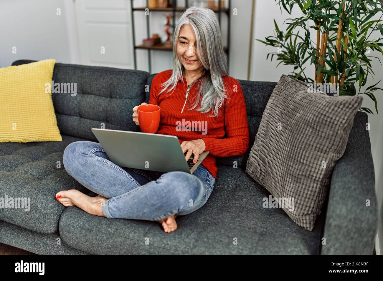 Middle age grey-haired woman drinking coffee using laptop at home Stock ...