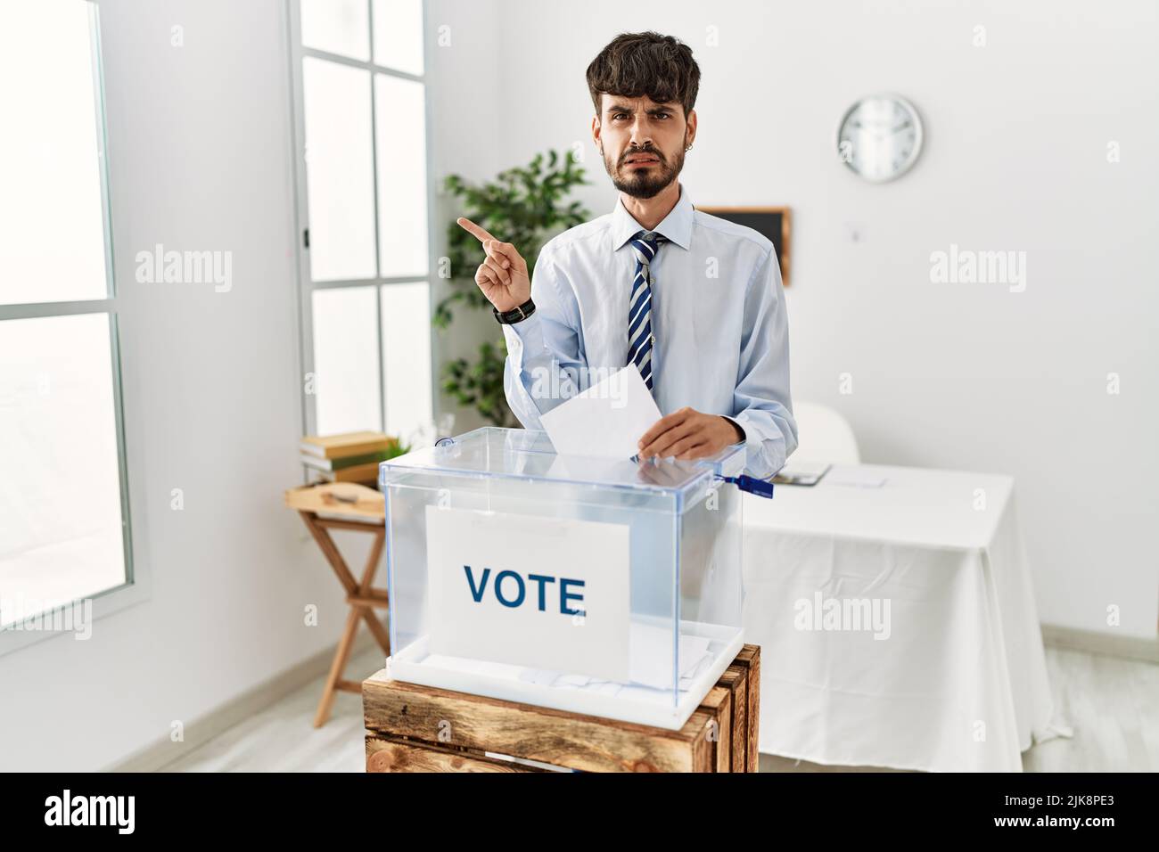 Hispanic man with beard voting putting envelop in ballot box pointing ...