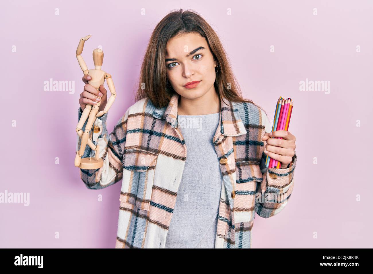 Young caucasian girl holding small wooden manikin and pencils relaxed ...