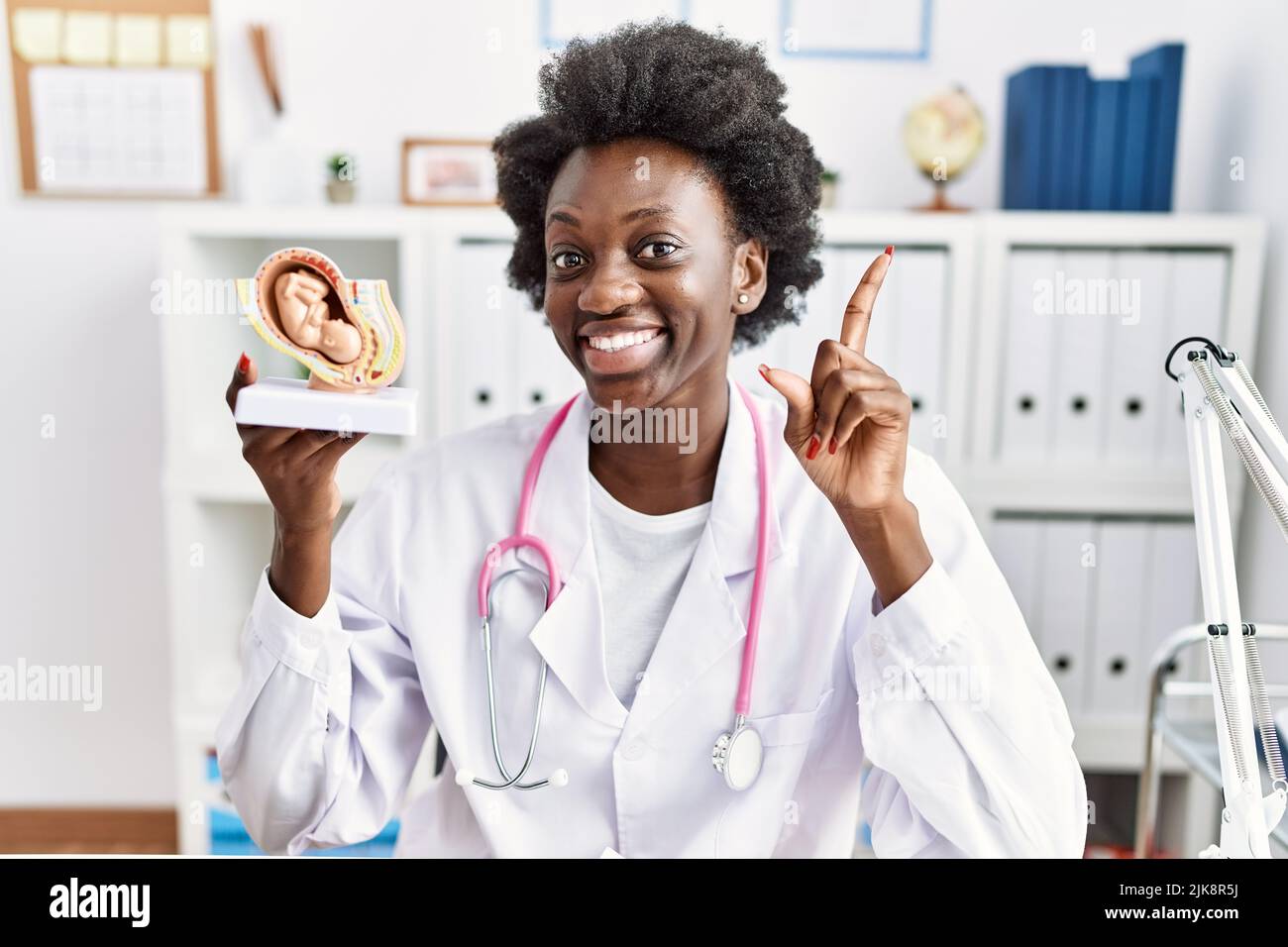 African doctor woman holding anatomical model of female uterus with fetus surprised with an idea ...
