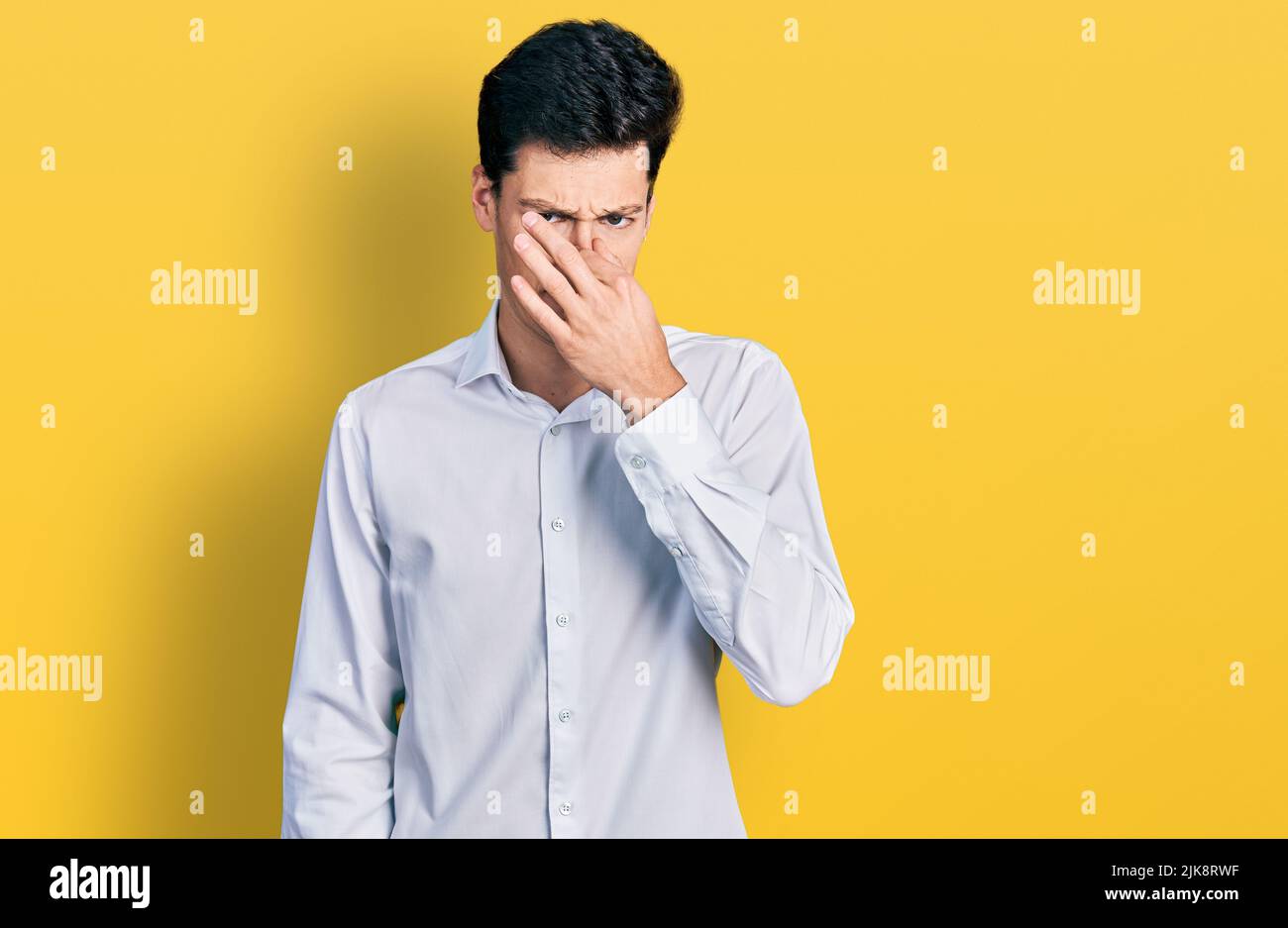 Young hispanic business man wearing business clothes smelling something ...