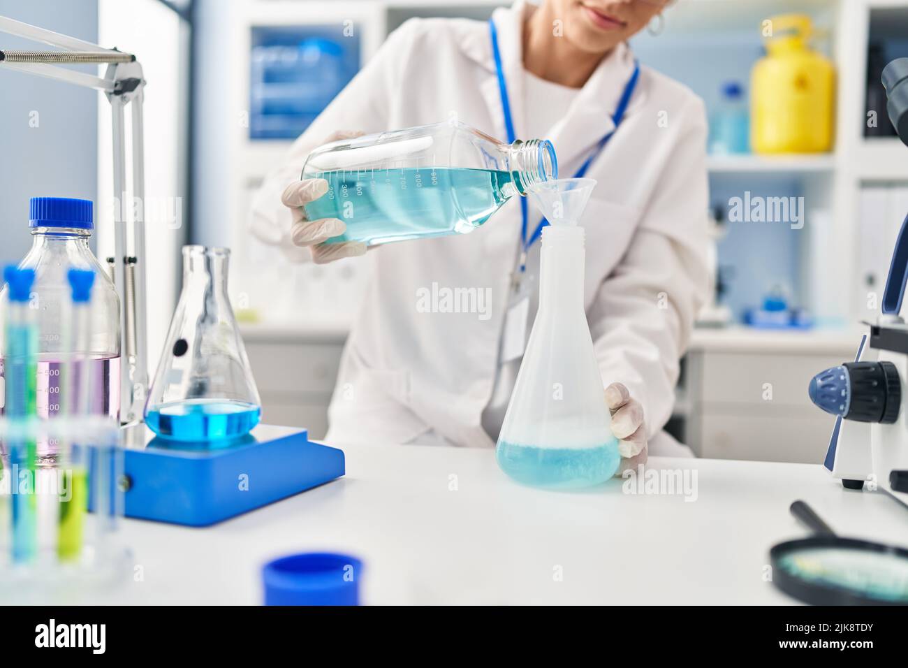 Young hispanic woman wearing scientist uniform measuring liquid at ...