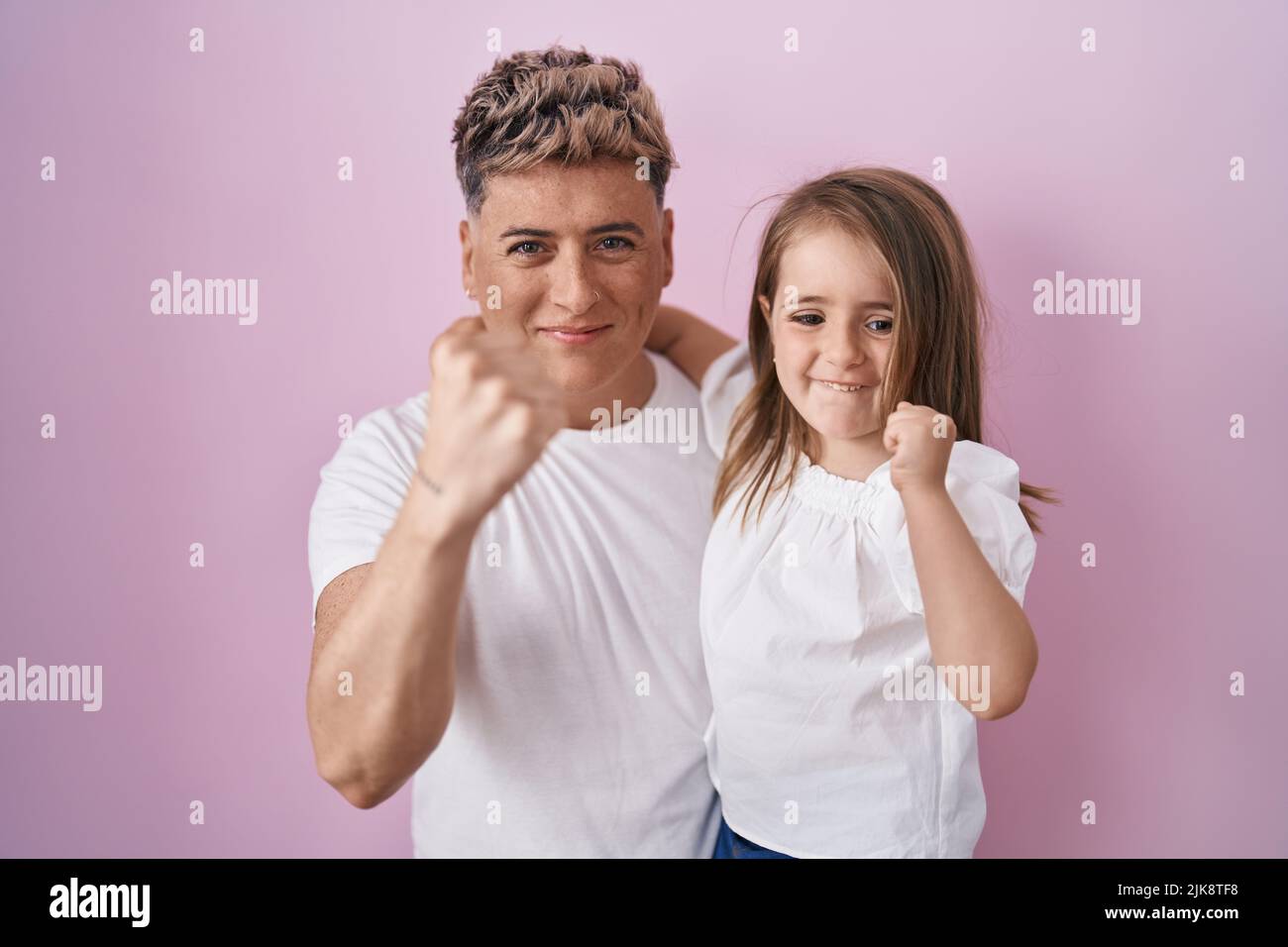 Young father hugging daughter over pink background annoyed and ...