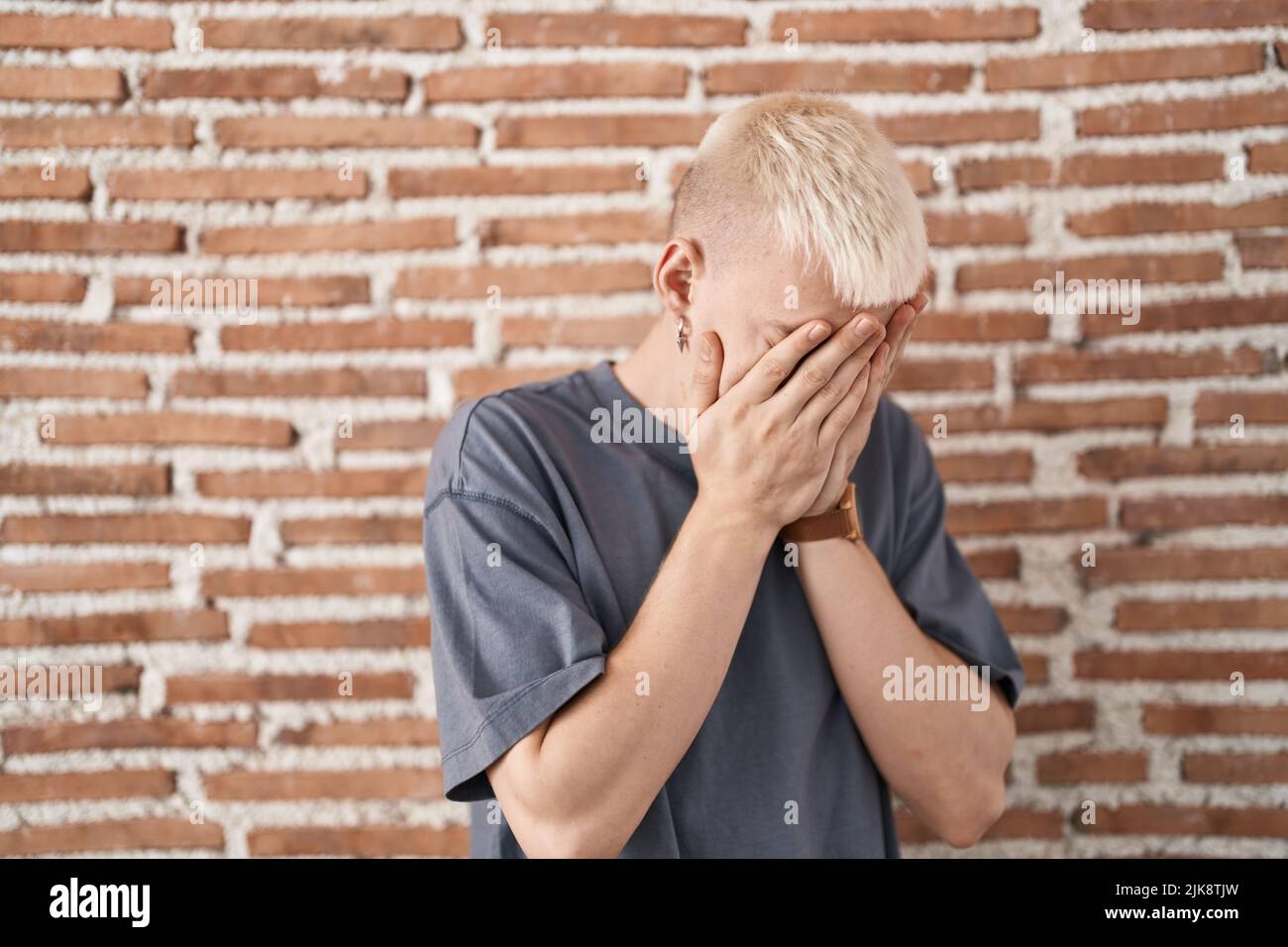 Young caucasian man standing over bricks wall with sad expression ...