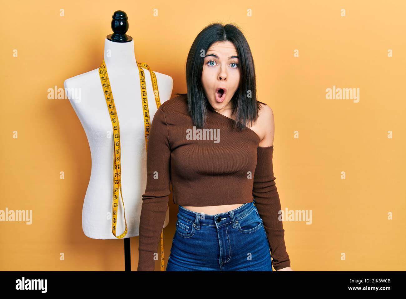 Young brunette woman standing by manikin scared and amazed with open ...