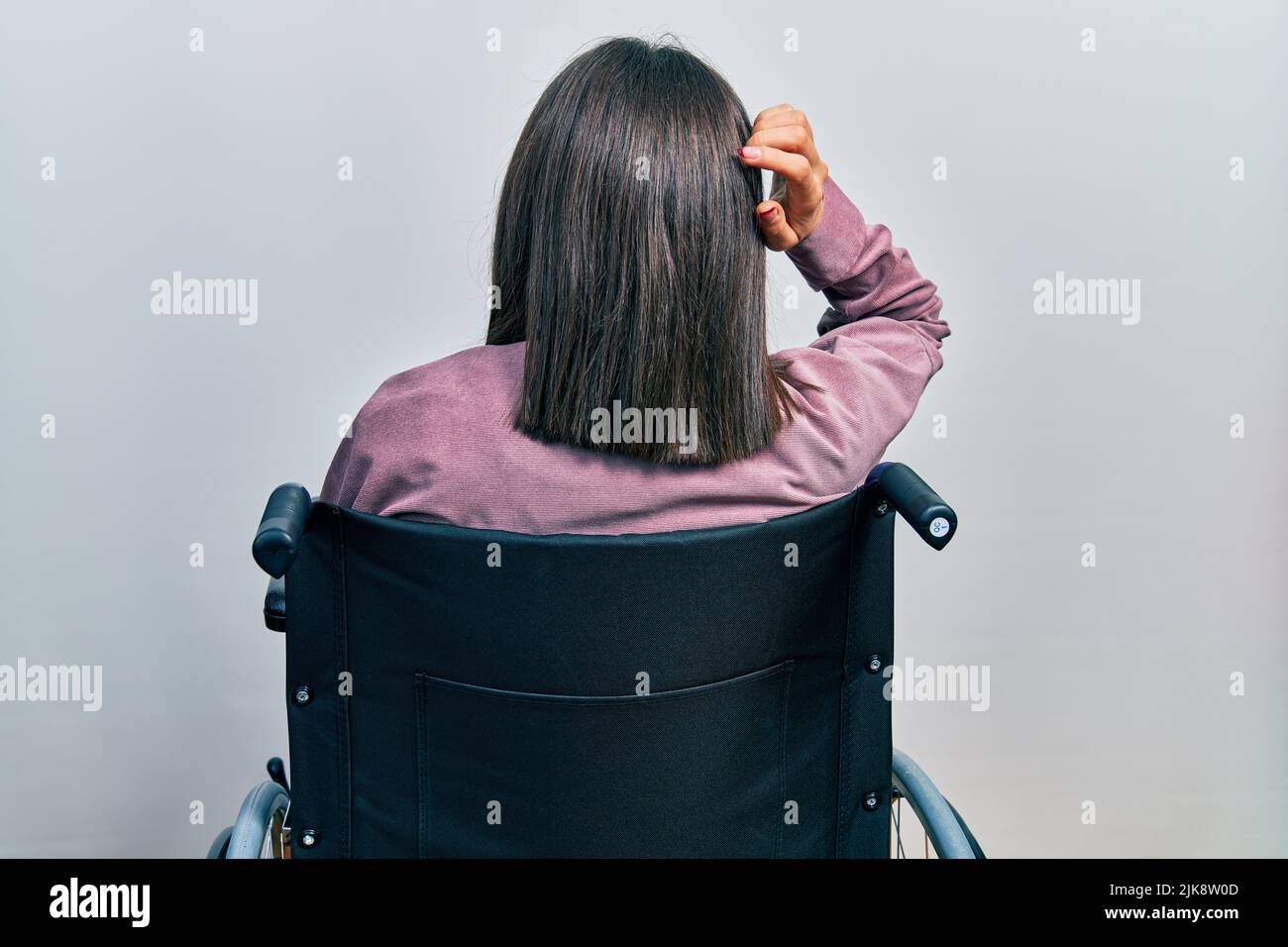 Young brunette woman sitting on wheelchair backwards thinking about ...