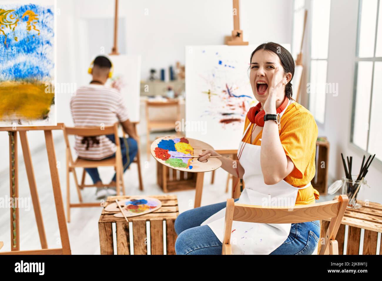Young artist woman painting on canvas at art studio shouting and ...
