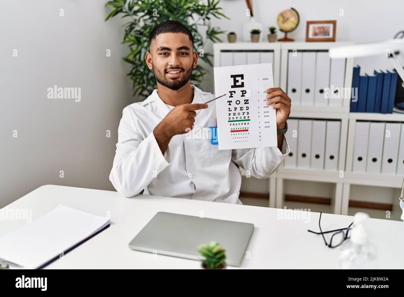 Young middle east man wearing optician uniform testing vision at clinic ...