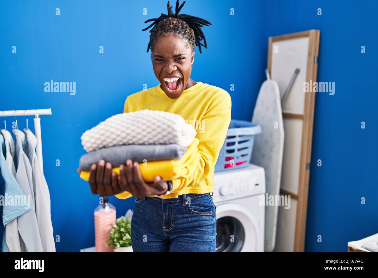 Beautiful black woman holding clean laundry angry and mad screaming ...