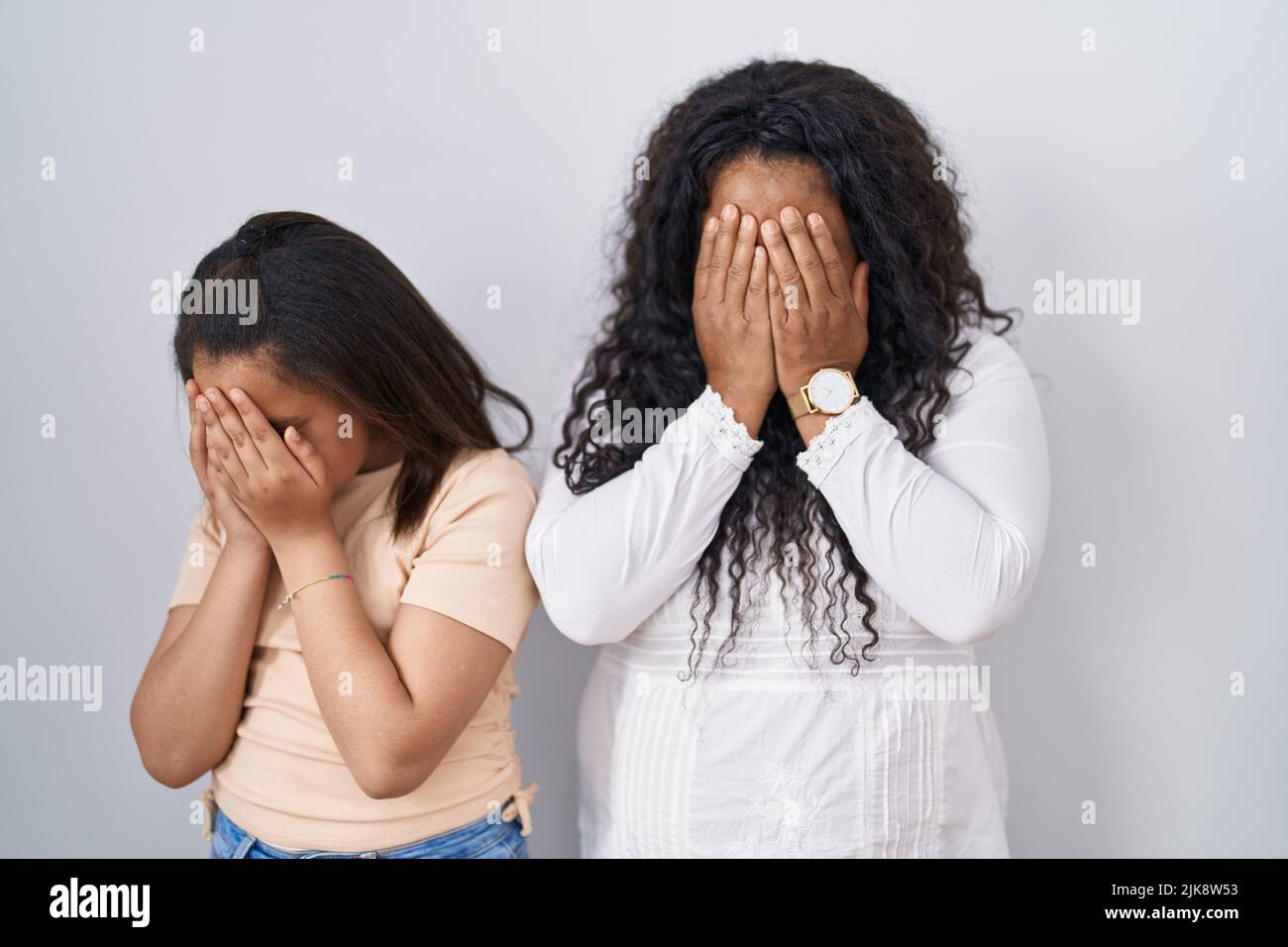 Mother and young daughter standing over white background with sad ...