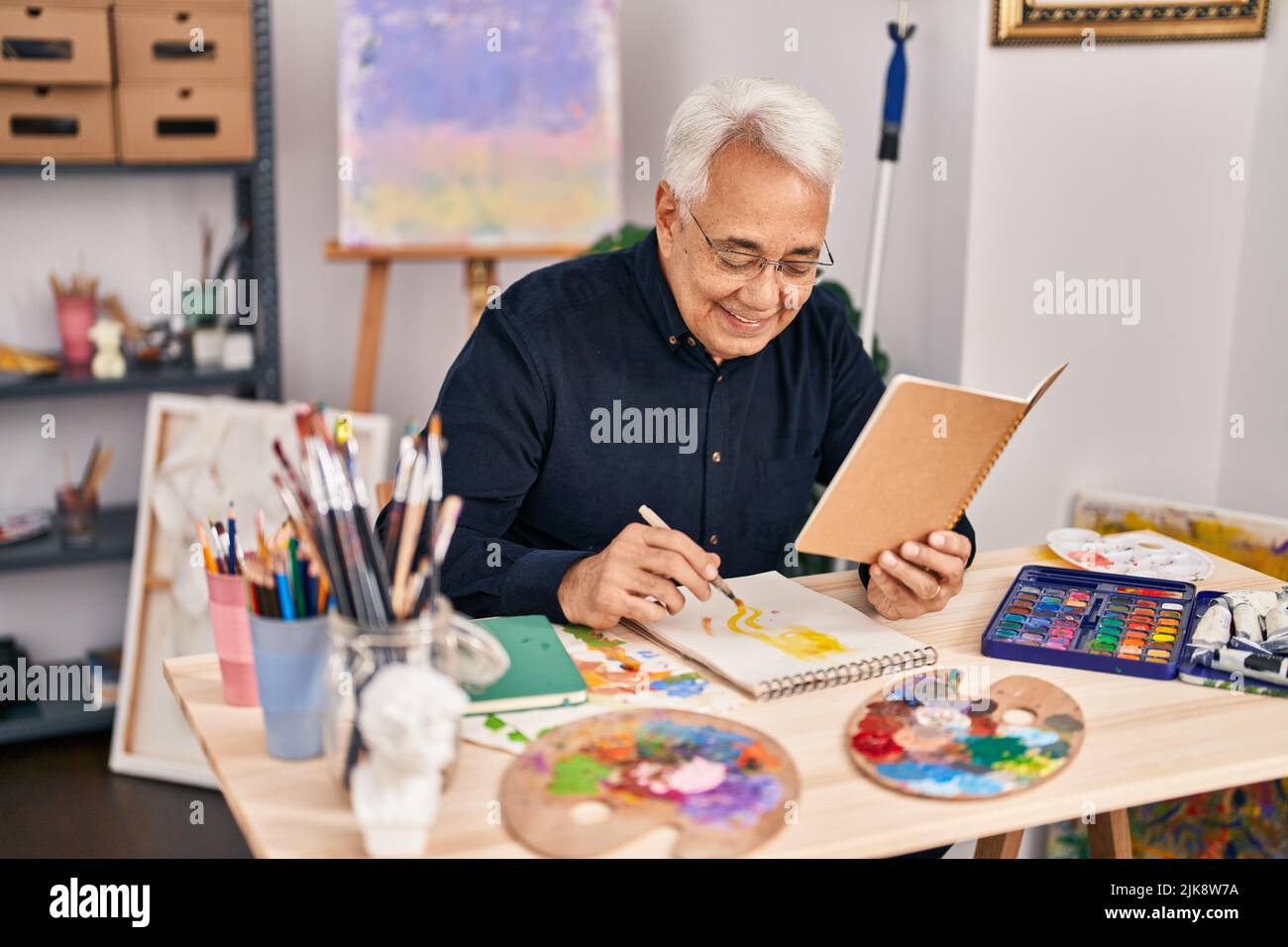Senior man drawing on notebook reading book at art studio Stock Photo ...