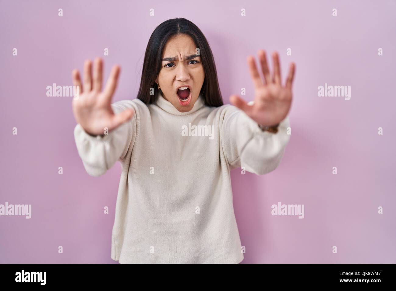Young south asian woman standing over pink background doing stop ...
