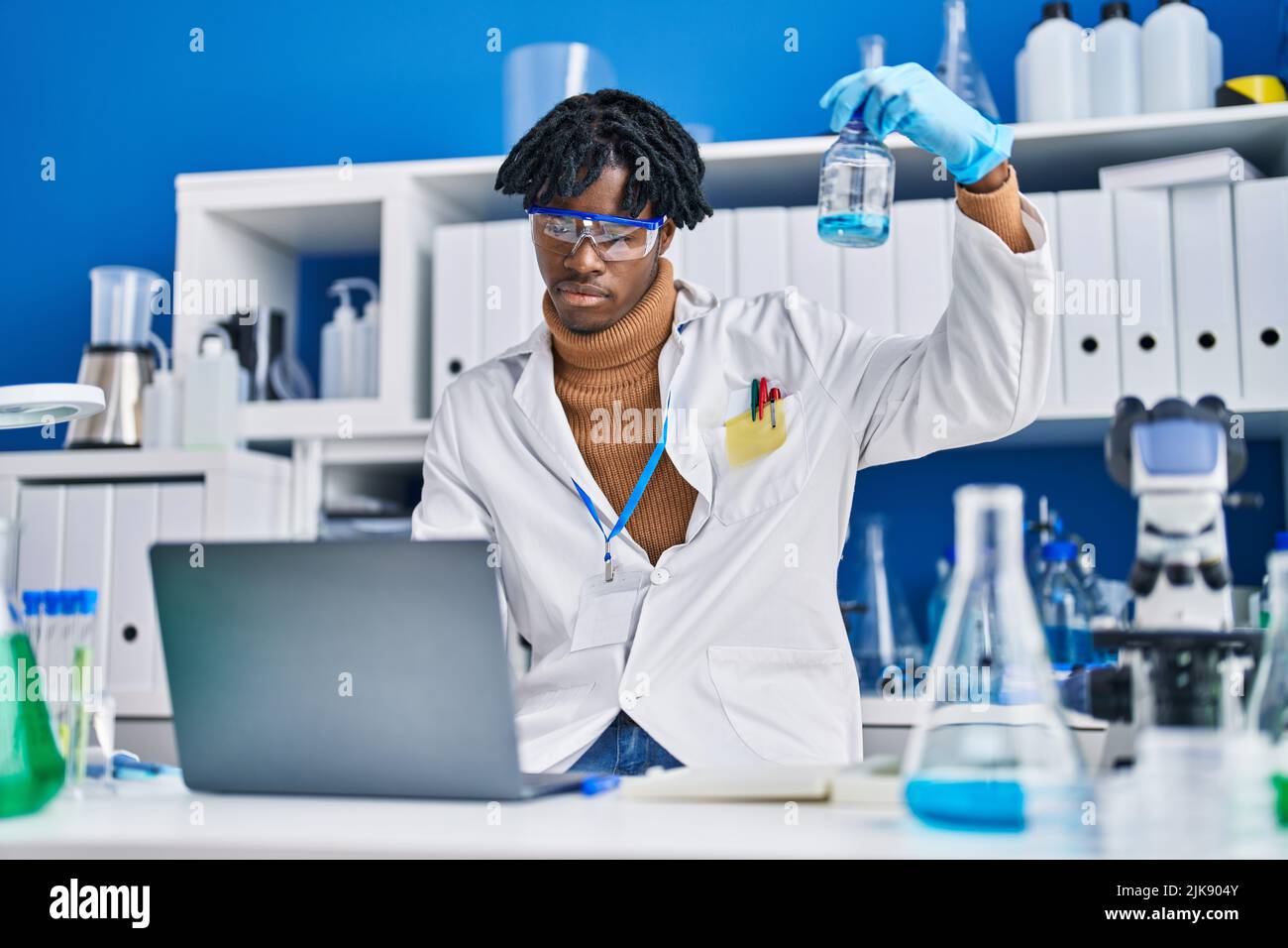 African american man scientist using laptop measuring liquid at ...