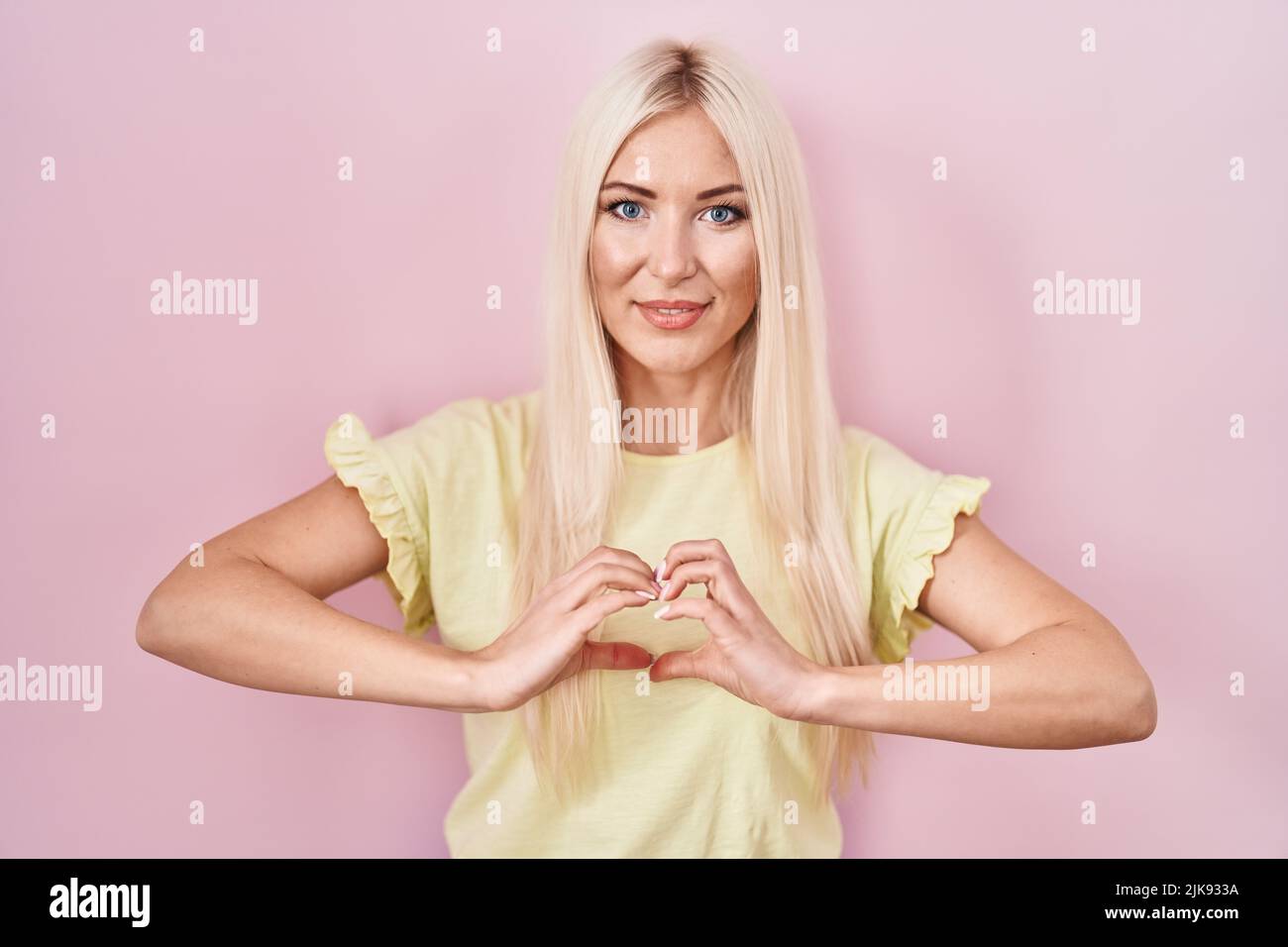 Caucasian woman standing over pink background smiling in love doing ...