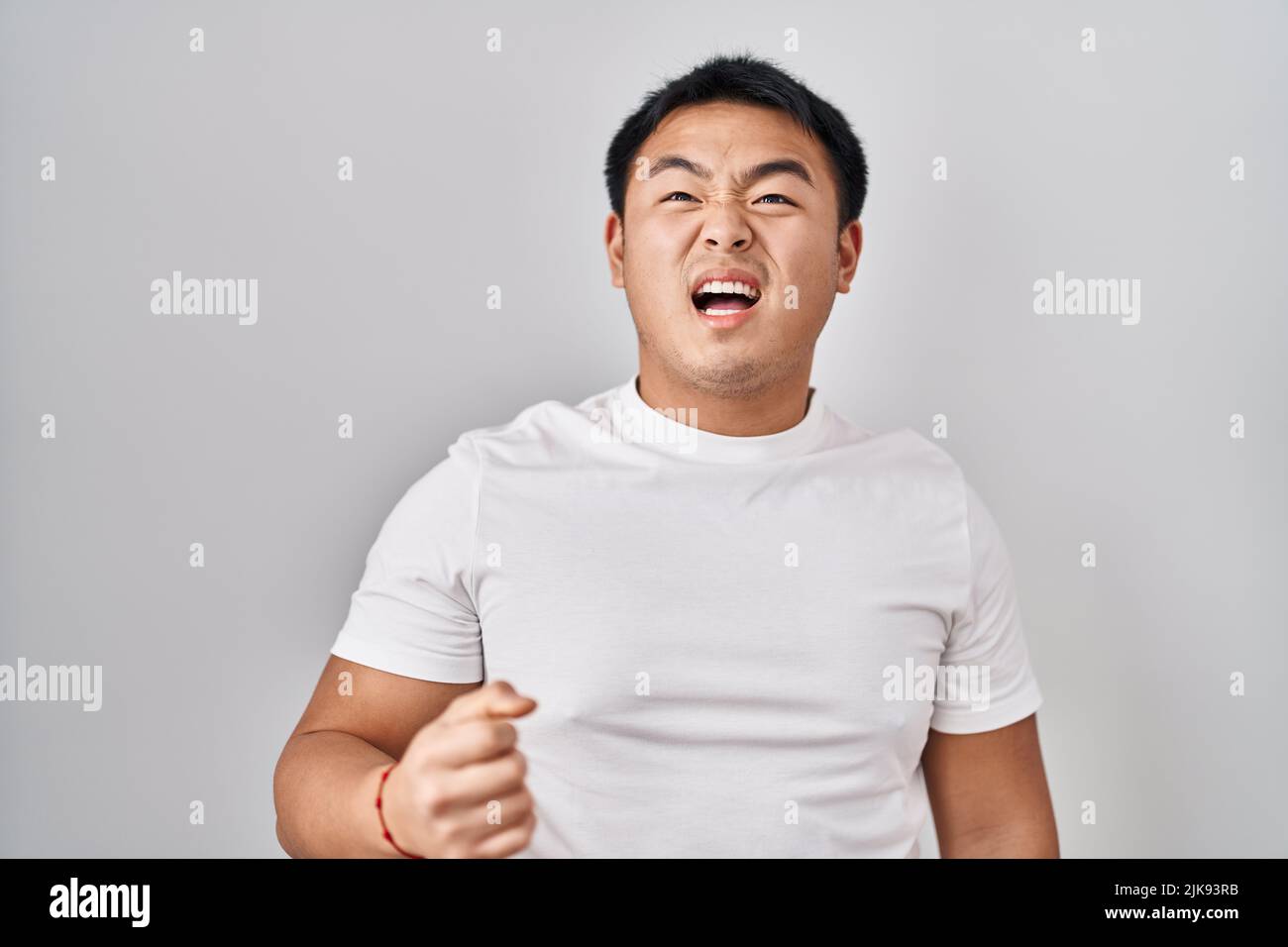 Young chinese man standing over white background angry and mad ...