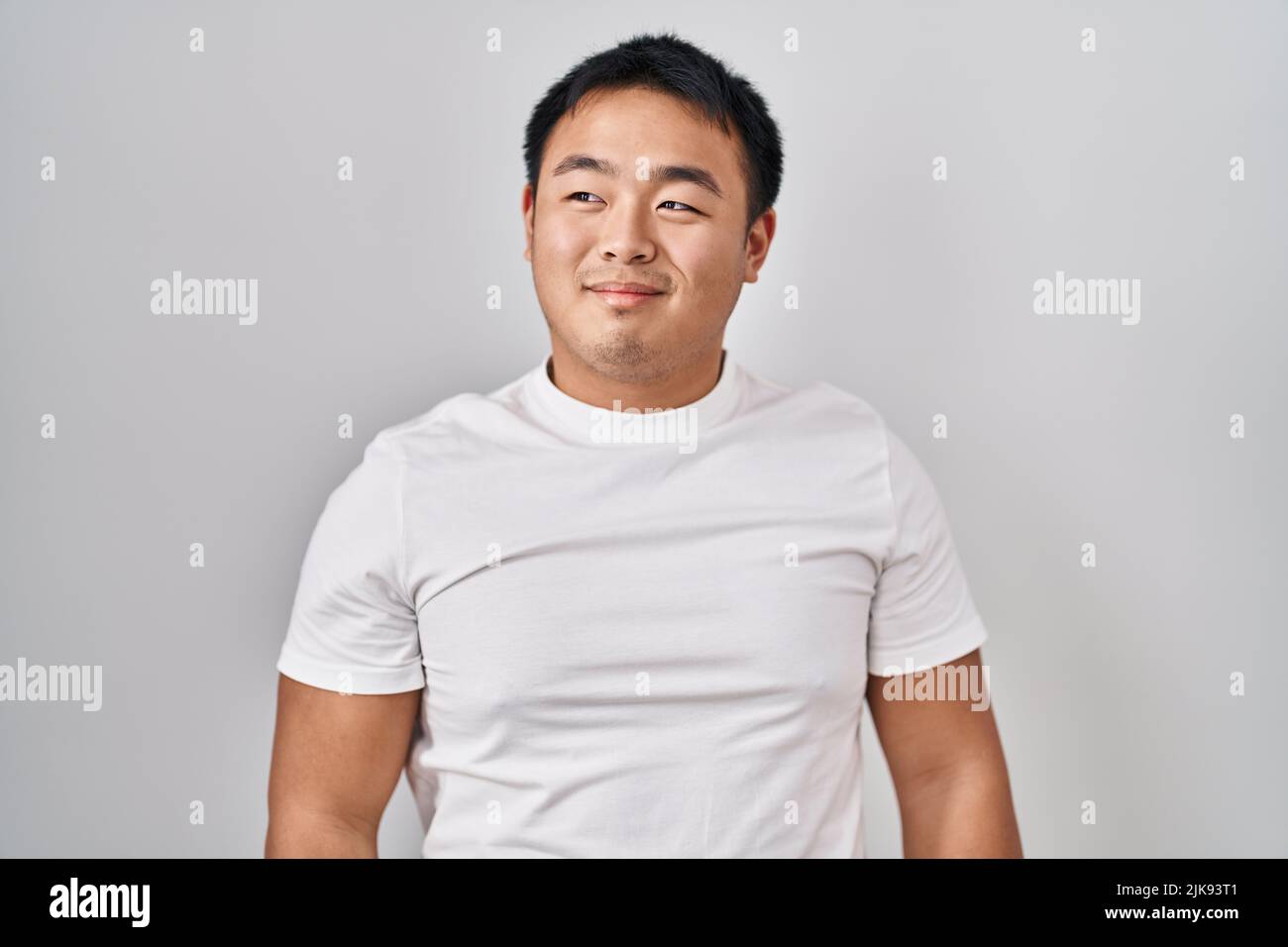Young chinese man standing over white background smiling looking to the ...