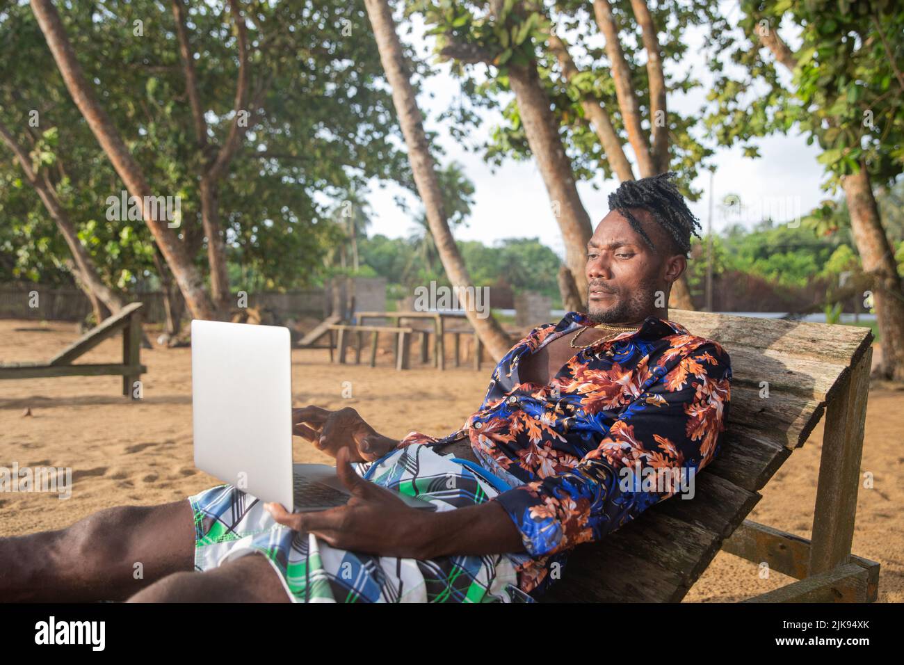 A digital nomad consults his computer while lying on the bench by the ...