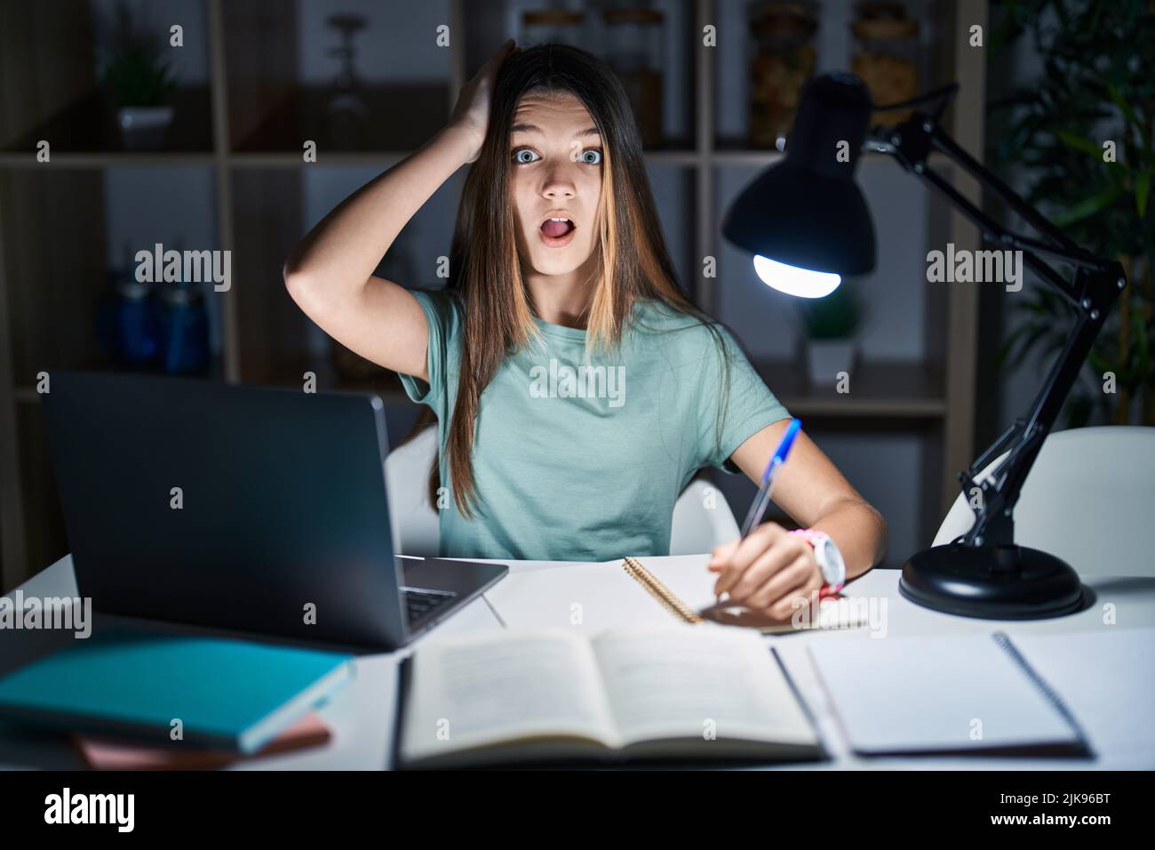 Teenager girl doing homework at home late at night crazy and scared with hands on head, afraid ...