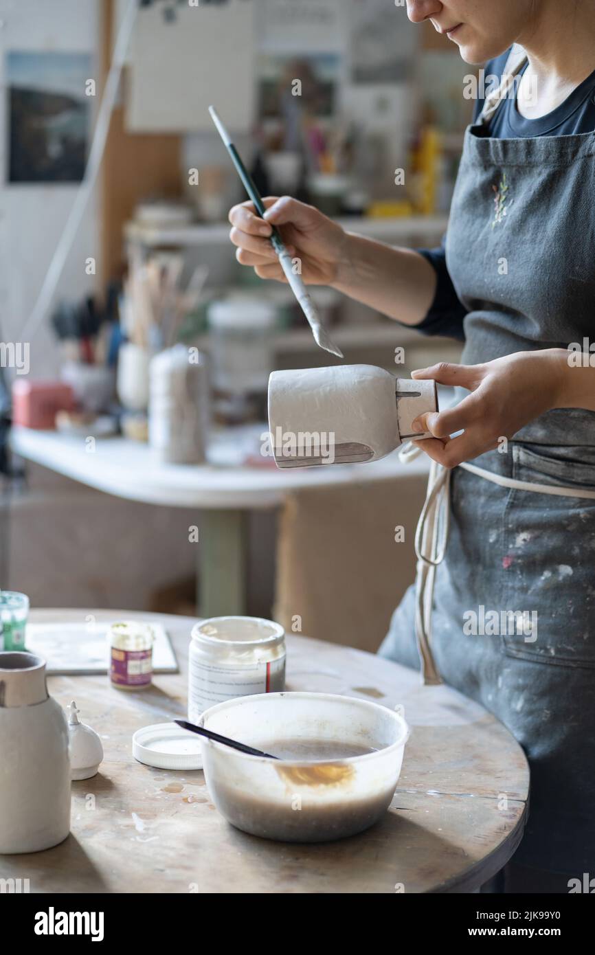 Young craftswoman paints vase with paintbrush after baking and handmade ...
