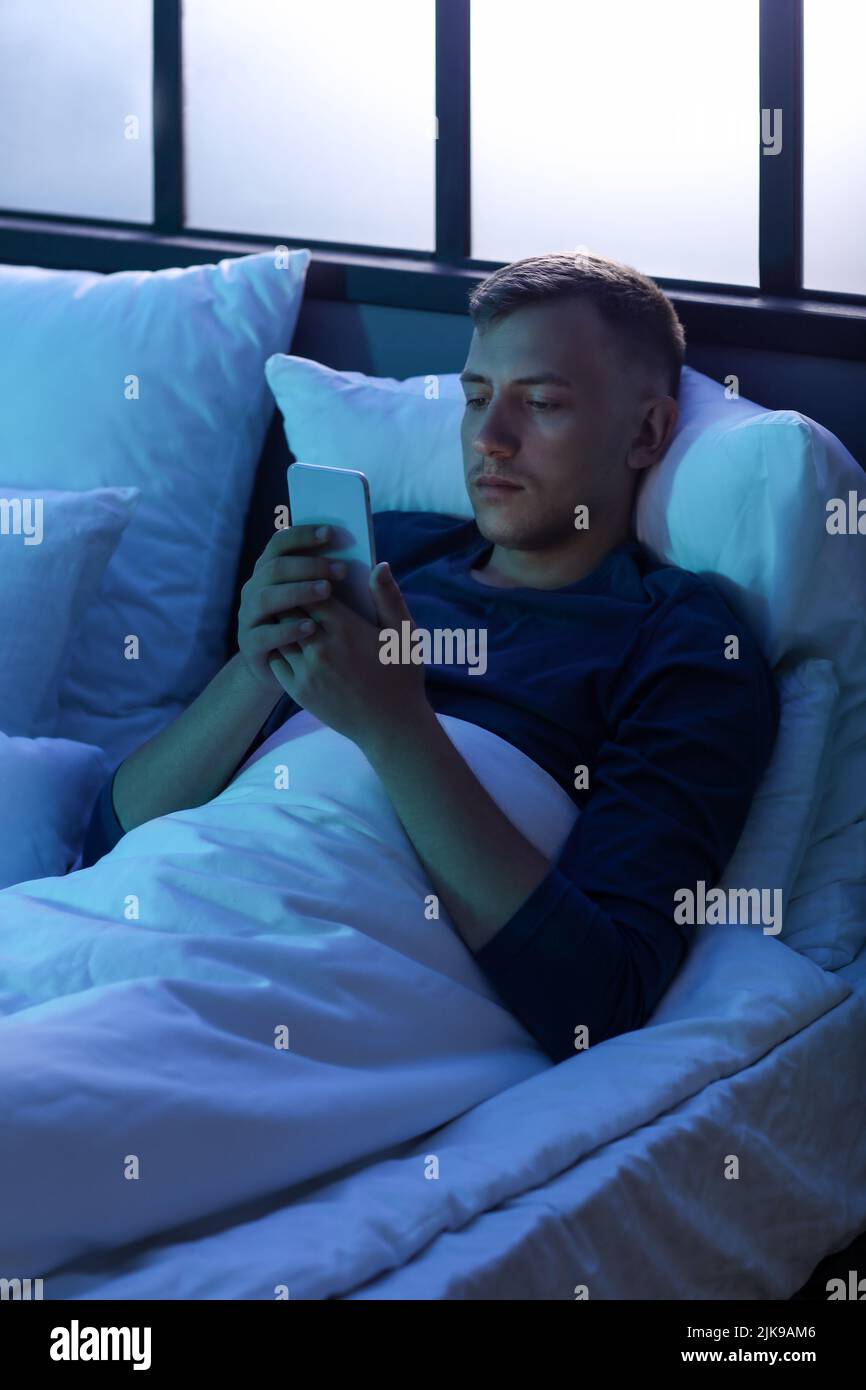Young man using mobile phone in bedroom at night Stock Photo - Alamy