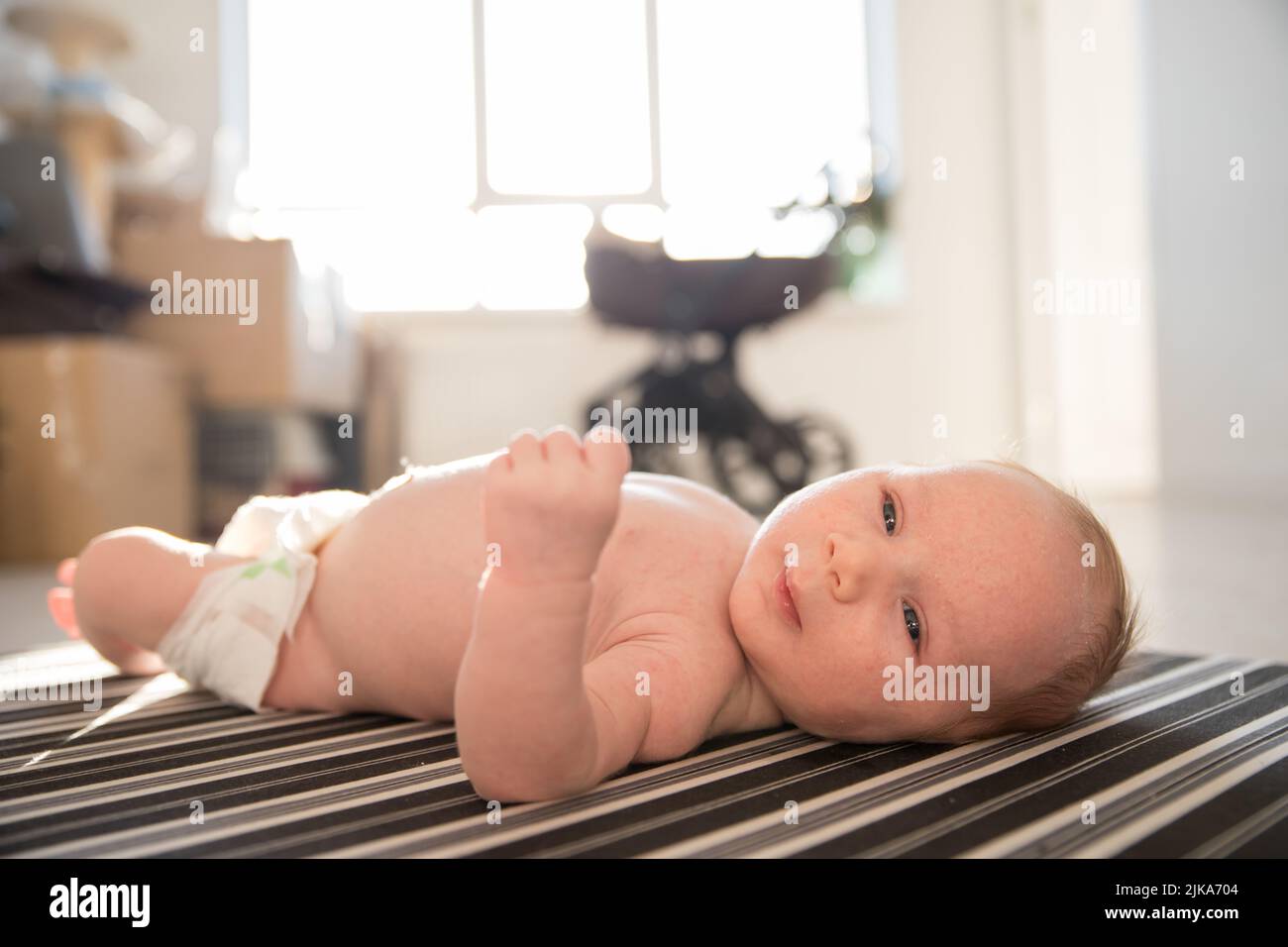 A little cute baby restlessly lying on his back on striped sheets in ...