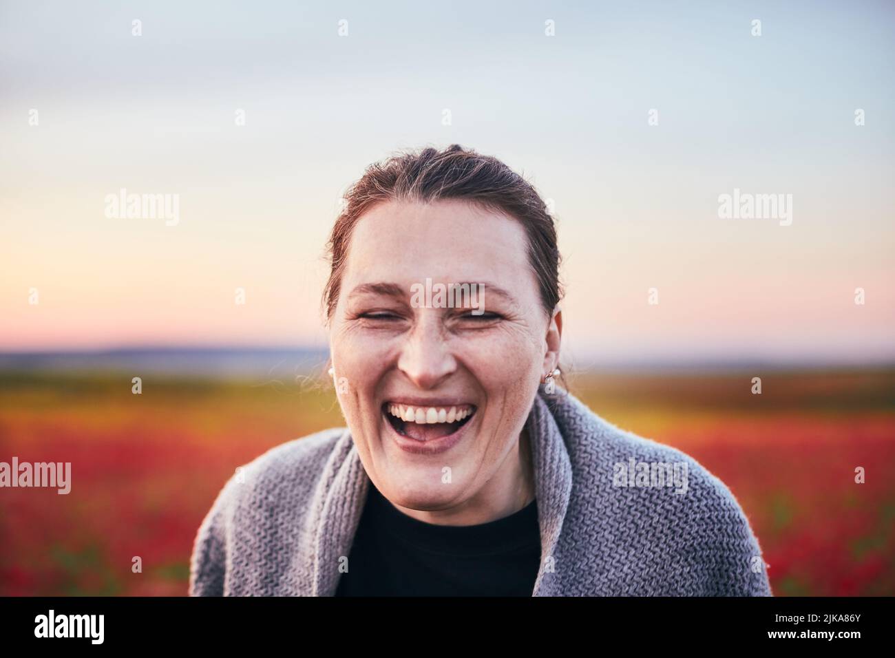 Portrait of a laughing woman in a poppy field at sunset. Front view ...