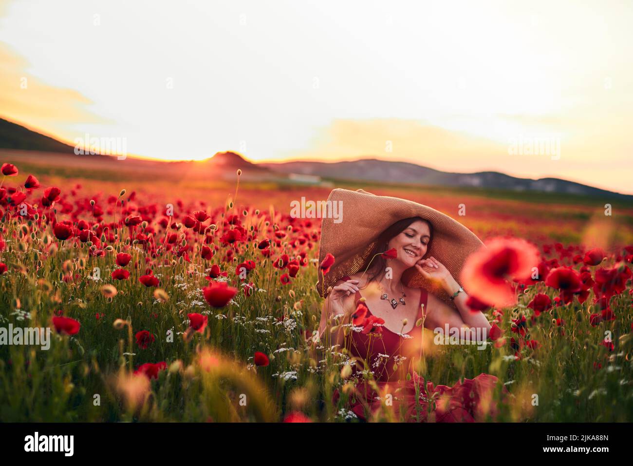 Portrait of a woman in a poppy field wearing a wide-brimmed hat at ...