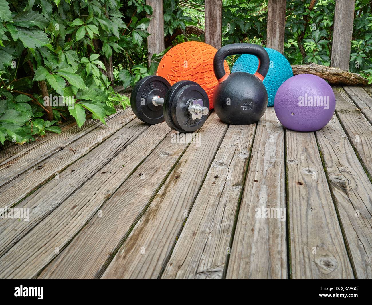 three heavy slam balls, iron kettlebell and dumbbell on a backyard deck ...