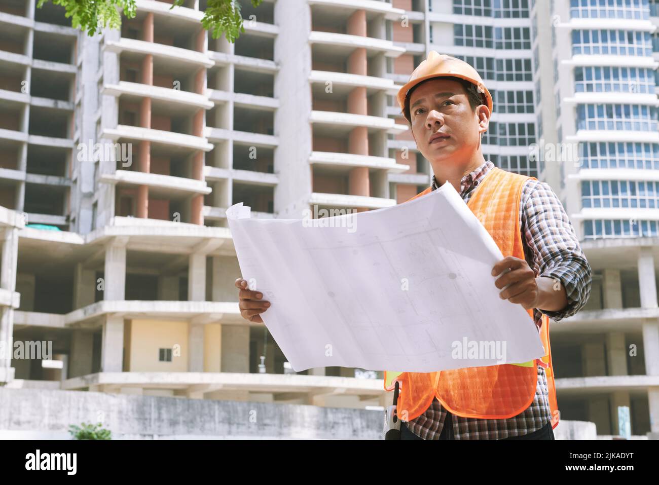 Portrait of architect with blueprint standing in front of building ...