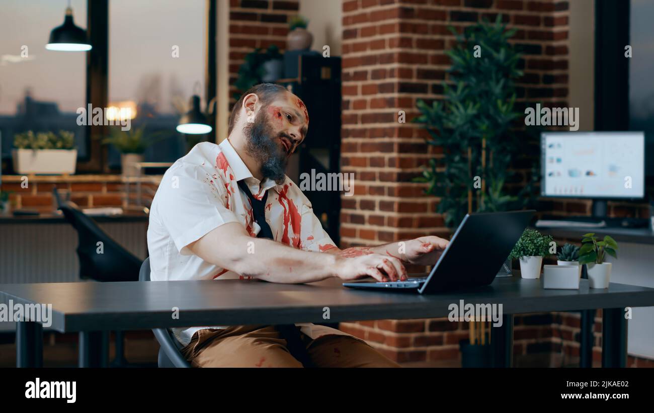 Scary looking zombie trying to work on modern laptop in office ...