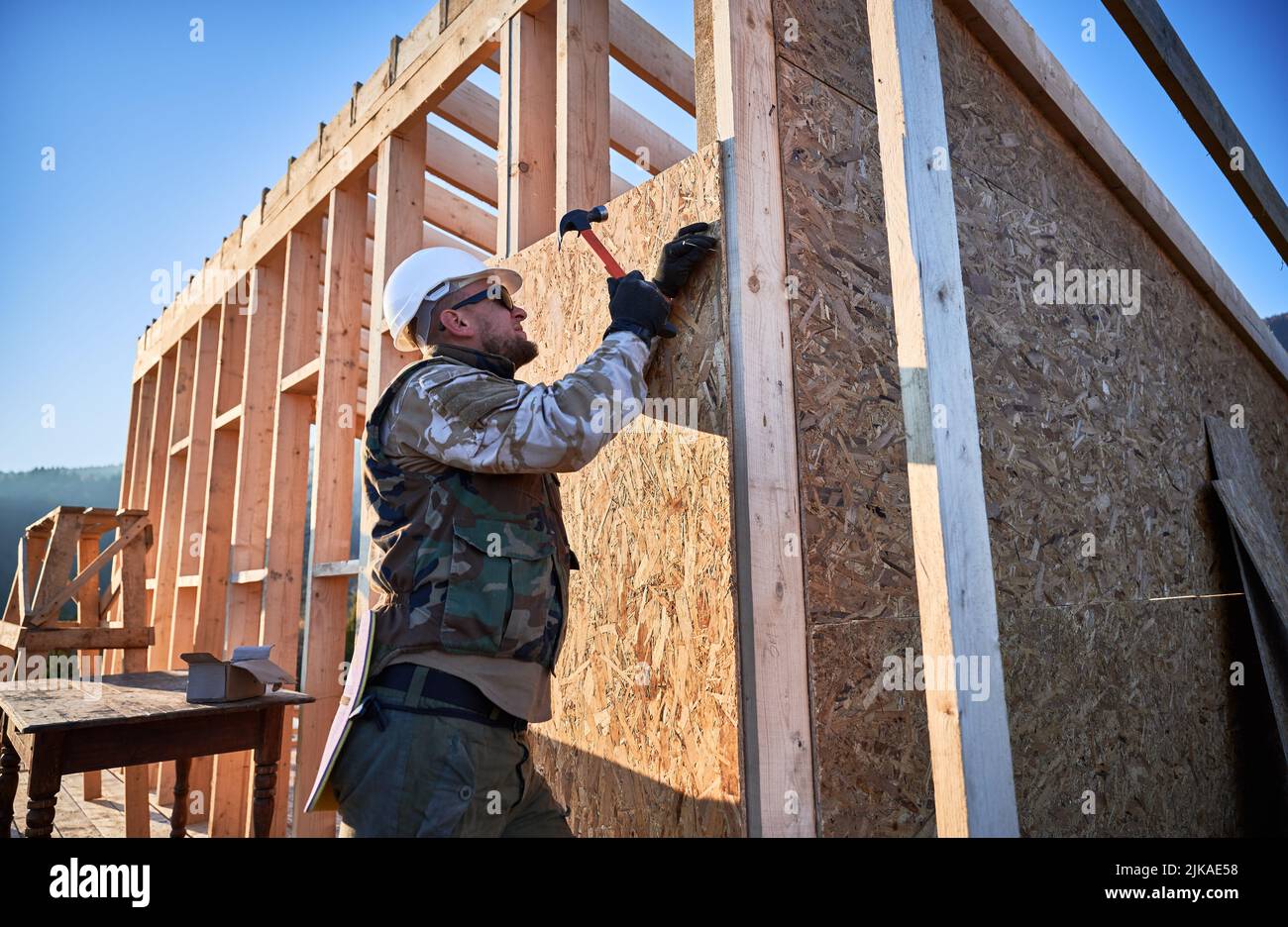 Carpenter hammering nail into OSB panel on the wall of future cottage ...