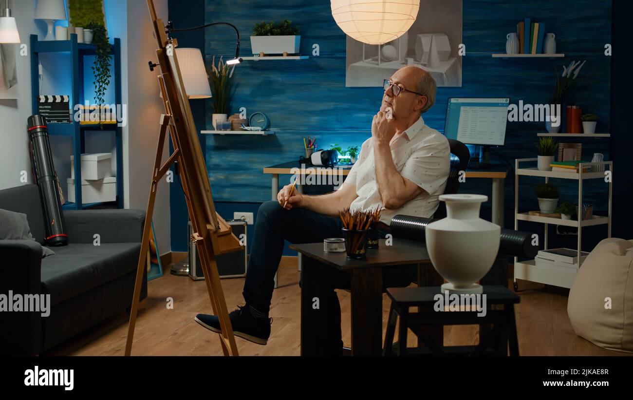 Senior artist looking at vase model to draw on canvas, using hobby and ...