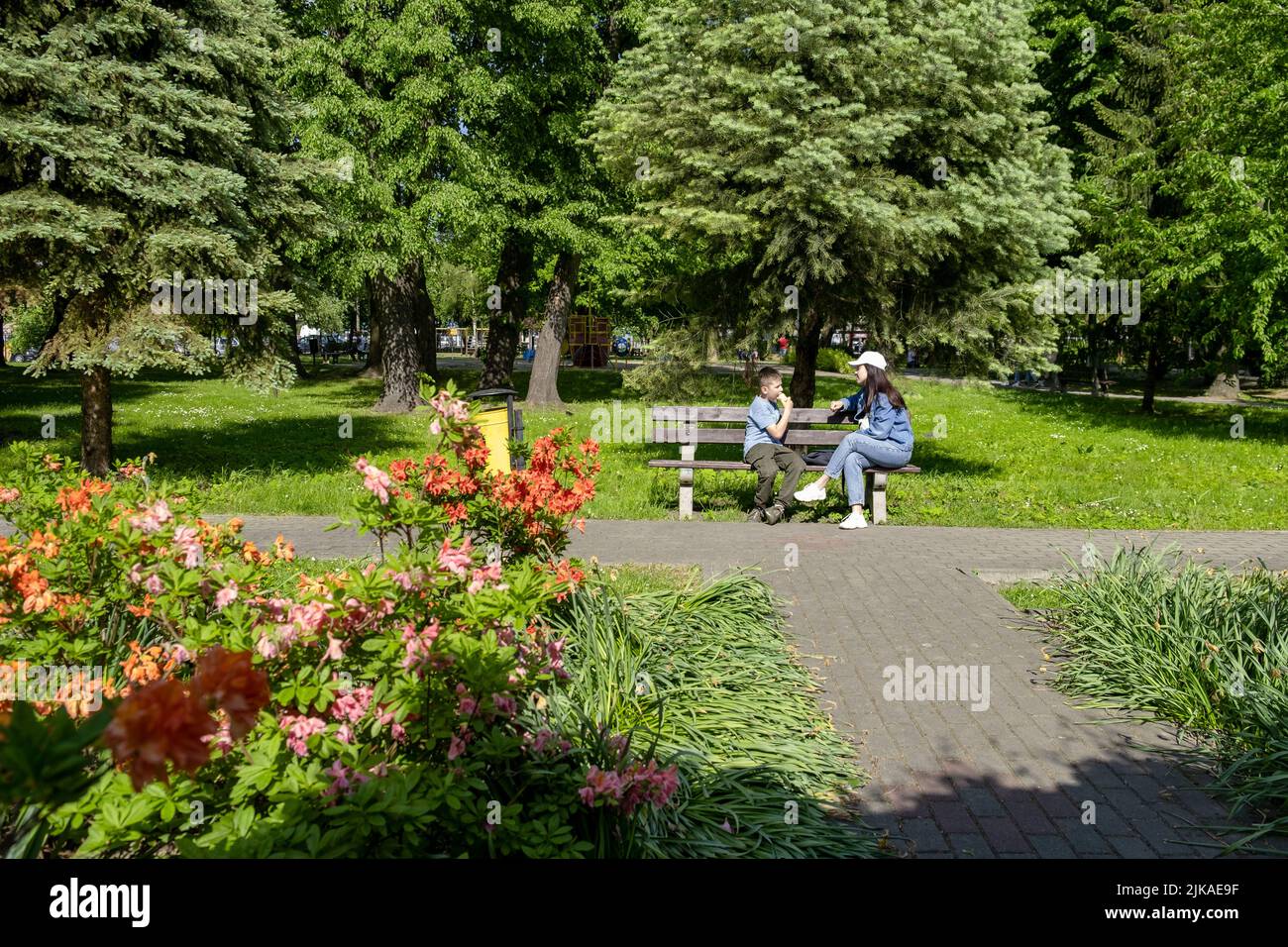 woman with kid sitting on the bench at public park. boy eating ice ...
