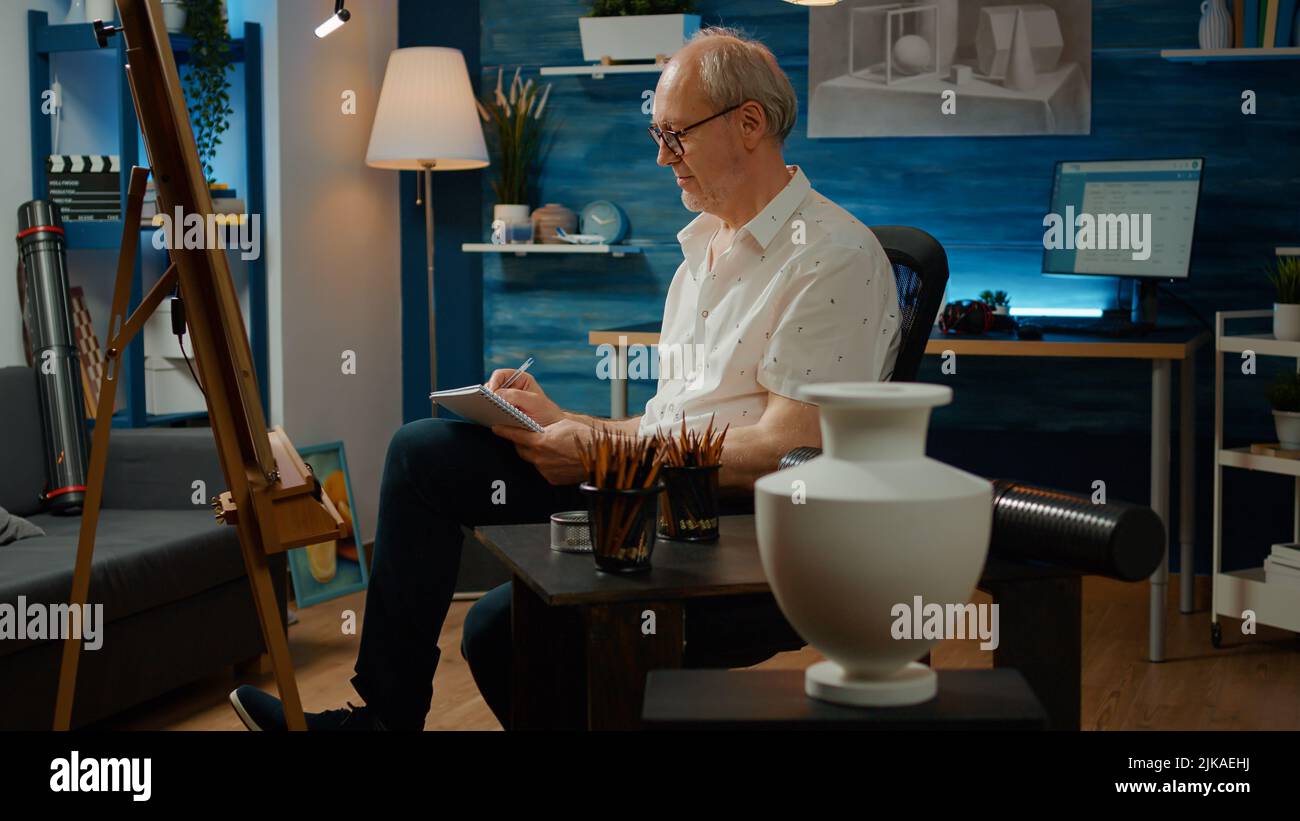 Old creative artist taking notes on paper to draw vase model sketch ...