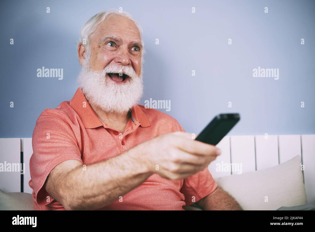 Excited senior man with white beard using remote control to switch ...