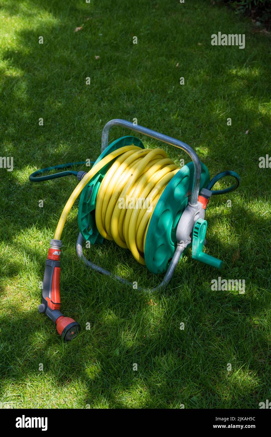 Garden hose fully wound on reel and standing on grass lawn in dappled ...