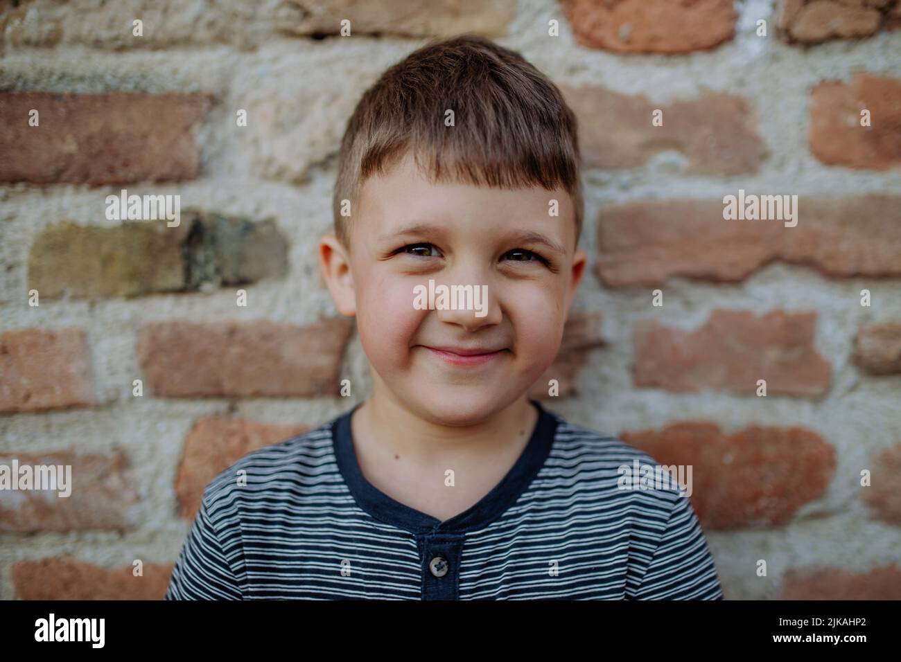 Little boy standing by brick wall and making funny faces in street ...