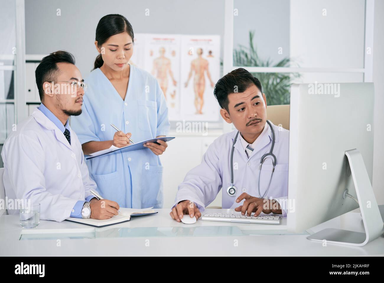 Team of doctors watching presentation on computer and taking notes ...