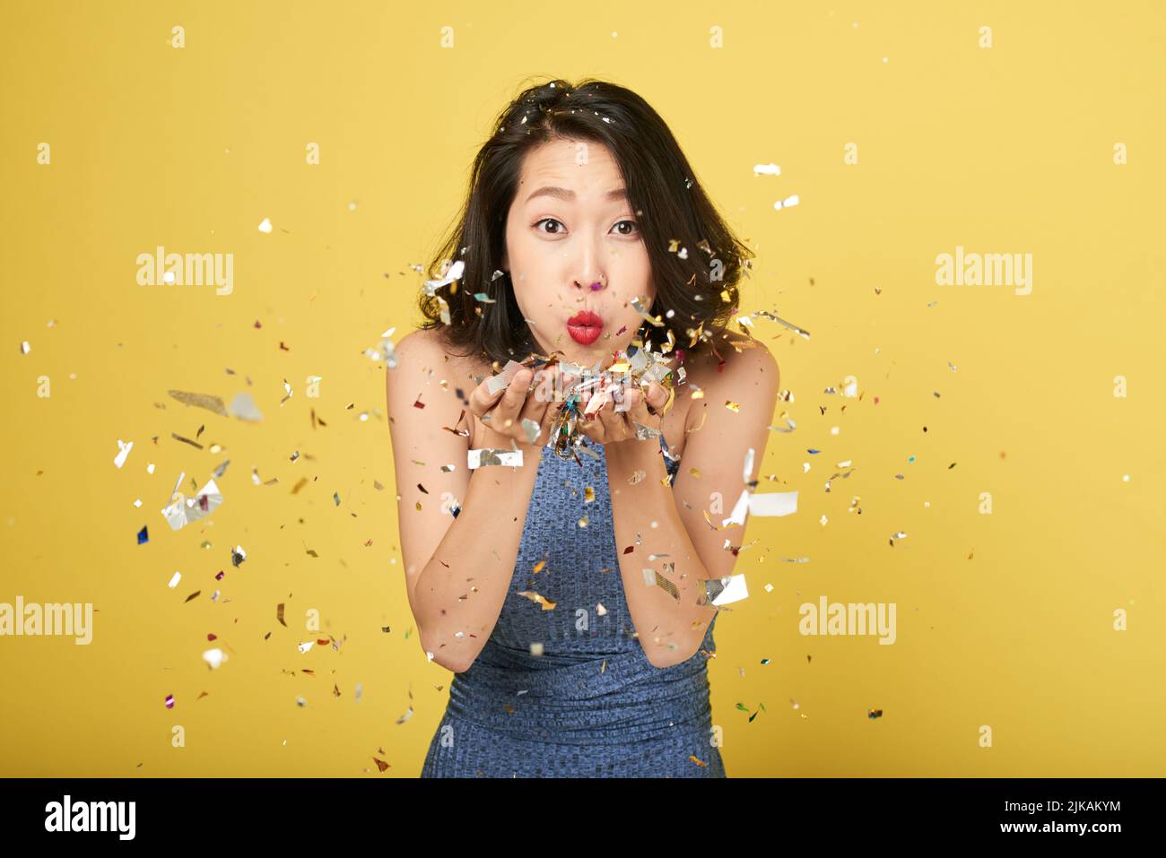 Cheerful young Asian woman blowing confetti into camera Stock Photo - Alamy